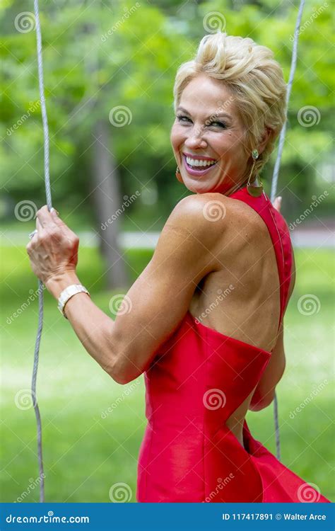 Gorgeous Blonde Model Posing Outdoors Wearing A Red Evening Gown Stock
