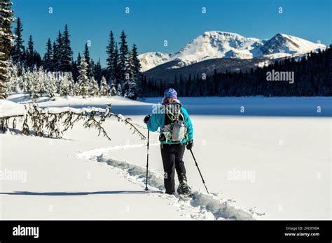 Female Snowshoeing On A Snow Covered Lake With Snow Covered Rocky