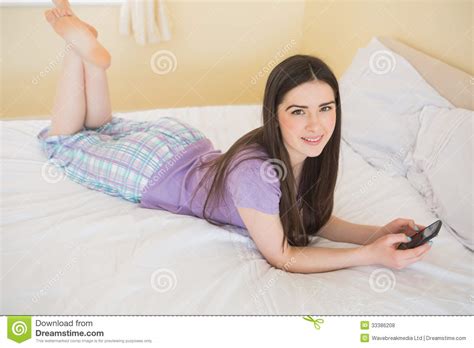 Muchacha Sonriente Que Mira La Cámara Y Que Miente En Una Cama Usando
