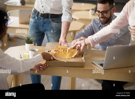 Happy Colleagues Enjoying Shared Pizza Lunch In Office Together Stock