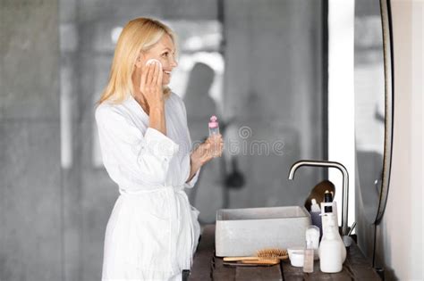 Smiling Mature Woman Wearing White Bathrobe Applying Refreshing Facial