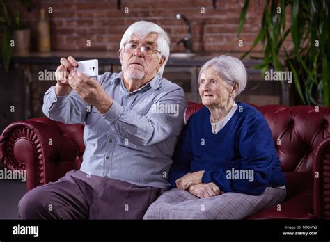 Senior Couple Taking Selfie On Smart Phone While Sitting On Couch At