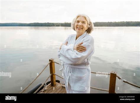 Portrait Of Happy Senior Woman Wearing White Bathrobe Hugging Self On