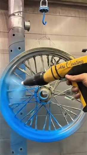 Spraying blue powder coating on a chrome motorcycle wheel with an electrostatic gun for restoration