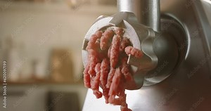 Meat coming through grinder plate. Closeup of minced meat flowing out of meat grinder. Slow motion blurred background kitchen. Advertising. Preparation of minced meat for hamburger by chef cook