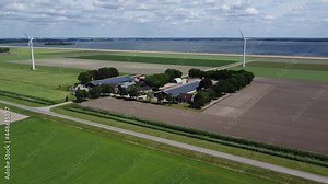 Aerial view of typical farm located at polder landscape showing pastures around the buildings and in background wind turbines providing renewable sustainable energy 4k high resolution footage