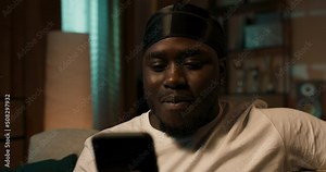 A man sits on the sofa with a smartphone in hand in spare time, browsing store websites, installing apps on phone, making an electronic shopping list, setting reminders in clanedar.