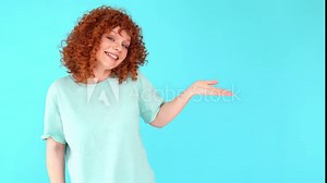 Positive young curly red-haired woman smiling pointing aside with hands at green copy space making suggestion and recommendation showing commercial advertisement workspace with empty place for text