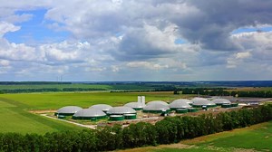 Download Agricultural plant for biogas production. Panoramic view on beautiful nature and biogas factory on it. Storage tanks for organic products among green field. for free