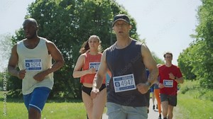 Slow Motion of a Diverse Group of People Running a Marathon in a City During the Day in a Green Park Trail. Resilient and Dedicated Joggers Racing to the Finish Line, Pushing Through Tiredness