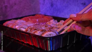 Sushi roll is taken with chopsticks for sushi close-up. Japanese cuisine sushi in a restaurant. Sushi roll with salmon and vegetables. Japan restaurant menu. Side view.