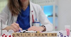 Woman physician sits at desk and completes prescription form. Pre-filled syringe and small box of Antihistamines shown on cubes put neatly on table
