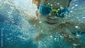 Male kid jumping to blue swimming pool bubbles water happy childhood underwater shot slow motion