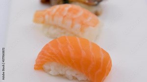 Chopsticks takes sushi with escolar from assorted sushi on a black plate on dark background. Minimal concept. High quality 4k footage