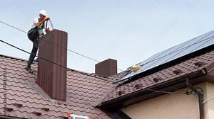 Workers installing solar panels system on rooftop of house. Electricians connecting cables from solar modules to inverter through the chimney for generating electricity through photovoltaic effect.