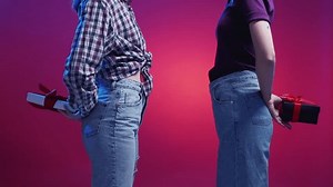 Present exchange. Female friends. Neon light people. Unrecognizable two women holding gift boxes hiding back posing blue magenta background.