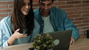 Couple greet friends in video call at home at the table. Modern people in chat conference online. Small internet business. Saying hallo to parents remote. Man and woman using laptop in indoor leisure