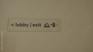 Navigation sign on beige wall of hotel corridor with direction of lobby and exit. Signs in English for tourists and hostel guests.