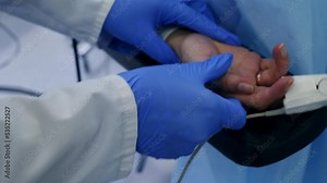 Nurse's hands in blue latex gloves put a sensor on female hand. Close up. Medic places patient's hand in the middle of the hand rest.