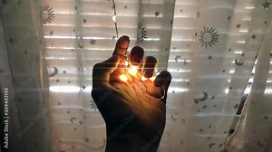 Hand with warm orange and yellow lights inside. Hands playing with small led lights in window with stars and moons curtains. Winter New year and Christmas Concept. Stock slow motion video.
