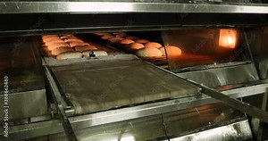A Baker Manually Pulling The Deck Oven Loader, Moving The Raw Bread Dough Into The Oven - Bread Making In A Bakery - Slow Motion