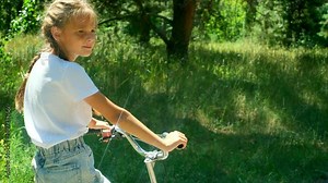 Little girl cyclist. Child rides bicycle, closeup. Child bike ride in nature, sun. Childs hands control bicycle handlebar. Child learns to ride bicycle. Sports lifestyle.