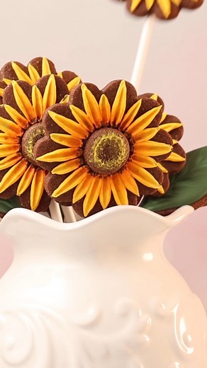 To turn these cookies into cookie pops, I cut a small scrap of cookie dough, brushed it with water, and pressed an oven-safe cookie stick into it. Then, I baked the cookie dough scrap with the stick and let it cool completely. Once it was cooled, I piped icing on the stick and pressed the decorated cookie on top of it so that the stick is in between the two cookies. This is a great way to turn any decorated cookie into a cookie pop! The full tutorial and recipes are in the Cookie Art Club. #swee