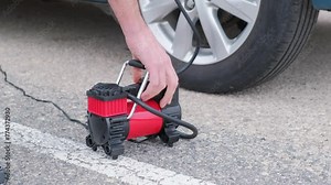 A man turns on a car air compressor to inflate tires.