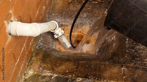 Professional plumber is pouring water into gully outside the house and cleaning pipe blockage under the ground by pushing sewer snake drain rod into sewer line