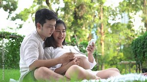 Happy Asian couple pregnant woman and husband using fetal doppler device for listening hear baby heartbeat device.