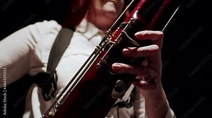 Female musician plays classical music on bassoon while sitting on chair in studio, dark background, front view. Female musician plays music at bassoon