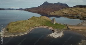4k aerial footage of ruins of Ardvreck Castle and Loch Assynt with mountains in background. Castle, clouds and sky reflected in calm water of loch. Panning around castle in circular movement.