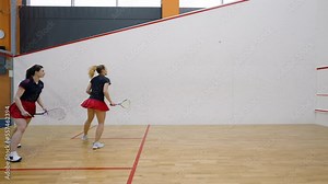 Female players alternate in striking squash ball with racket
