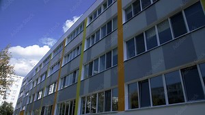 School building features large windows and minimalist facade. Well-kept flower beds line pathway creating pleasant atmosphere for students