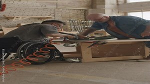Vertical full length shot of two professional woodworkers making chair seat upholstery on workbench in spacious wood workshop
