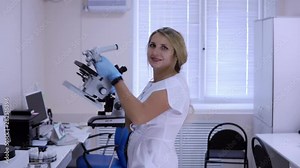 Beautiful blonde in a white medical gown dances merrily in a medical science laboratory with microscopes in her hands. Funny health worker biologist at work have fun and fool around.