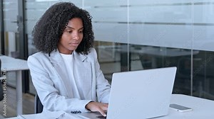 Middle age business woman working, browsing, and typing on touchscreen pc laptop. African American young female businesswoman, successful entrepreneur using app gadget sitting at work place in office.
