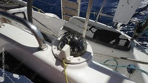 Closeup on left sailing boat compass and helm looking through steering wheel turning round. Electronic autopilot controls on a sailing yacht. Filmed on moving Sailboat Sailing Across The Blue Sea