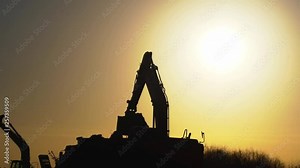 Silhouette of excavator. Dredge digs ground and loading tipper. Digger machine digging hole. Excavation of canal. Dump truck,tracked,bagger,backhoe,shovel,sunny blue sky,sun in background,backlight.