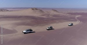 4K aerial zoom out view with beautiful scenery of a convoy of 4x4 vehicles driving through the sand dunes and mountains on the Skeleton Coast, Namib desert, Namibia