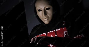 Male hacker hidden face with the mask accessing to personal information on laptop (phone) in the dark. Technology, cyber crime concept.