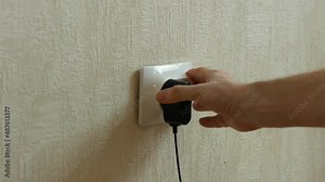 A man's hand inserts a charger into a faulty electrical outlet. Home electrical repair concept. An electrical outlet sticking out of the wall in the apartment.