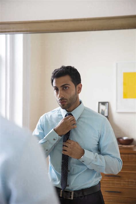 Man Adjusting Necktie While Standing In Front Of Mirror At Home Stock Photo