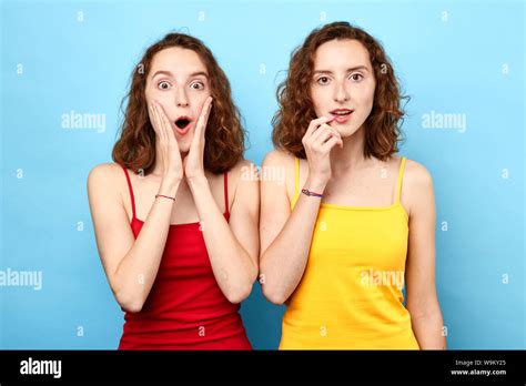 Puzzled Funny Sisters Looking At The Camera Making Faceswoman With Wide Open Mouth In Red Top
