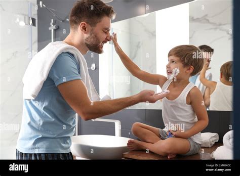Dad And Son With Shaving Foam On Their Faces Having Fun In Bathroom