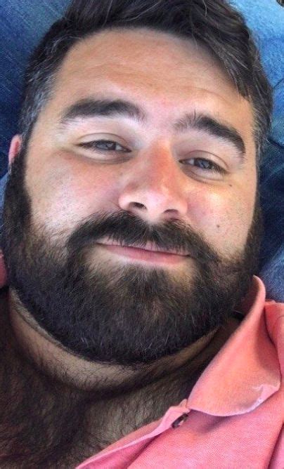 A Close Up Of A Person With A Beard And Pink Shirt On Sitting In A Chair