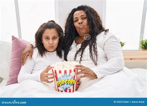 Mother And Young Daughter Eating Popcorn In The Bed Looking At The Camera Blowing A Kiss Being