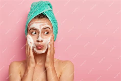 Free Photo Pretty Young Woman Washes Face With Soap Keeps Lips Rounded Looks Aside On Copy