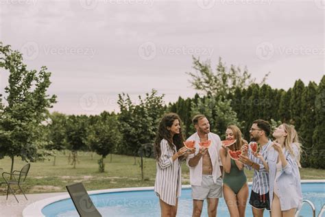 Young People Standing By The Swimming Pool And Eating Watermellon In The House Backyard 15709609