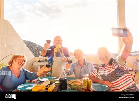 Happy Seniors Taking A Selfie With Mobile Phone And Making A Barbecue On The Rooftop Retired